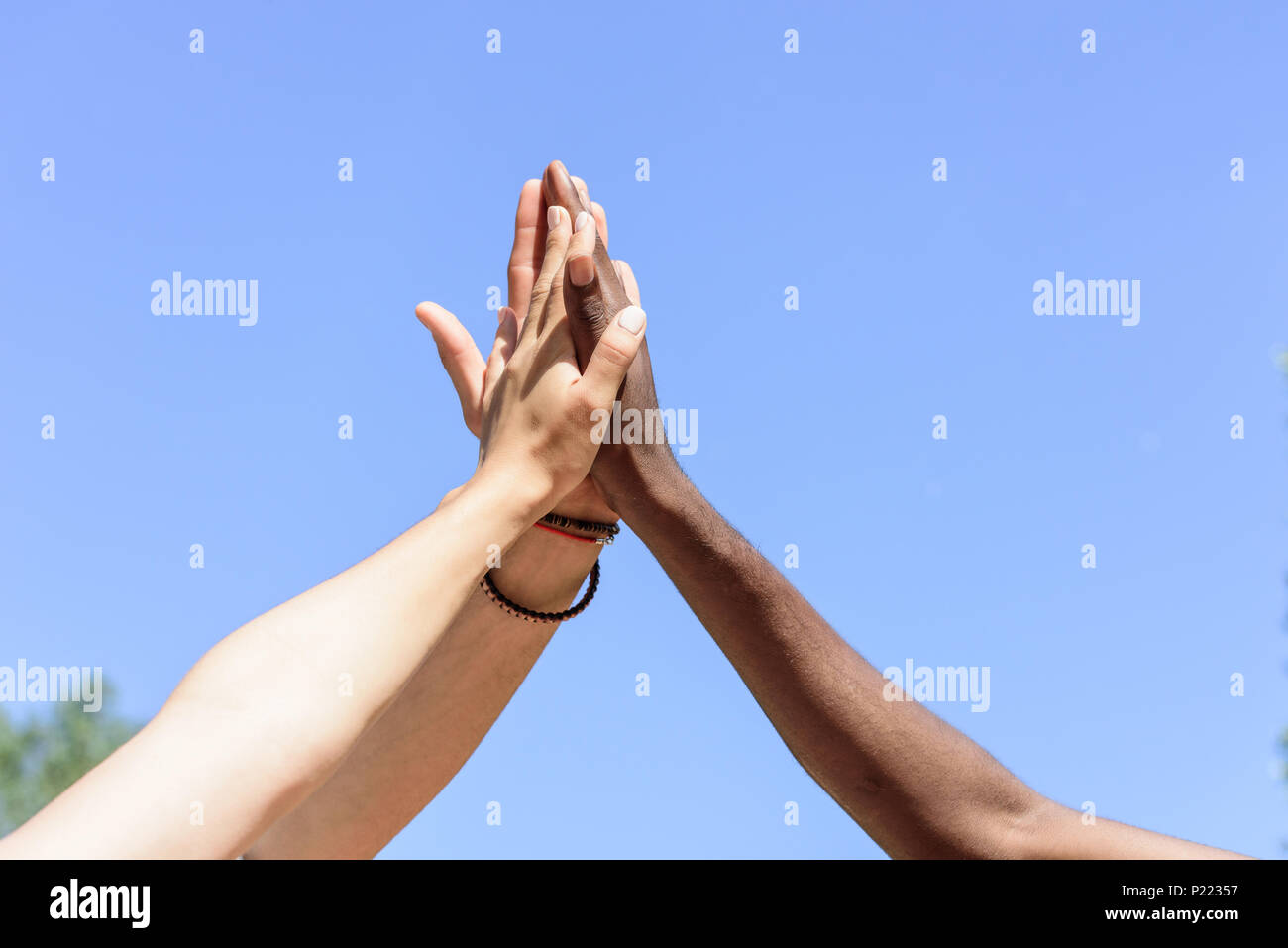 cropped shot of friends giving high five to each other against blue sky ...