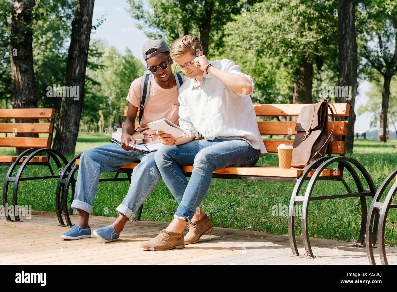 multicultural young students sitting on bench and studying in park ...