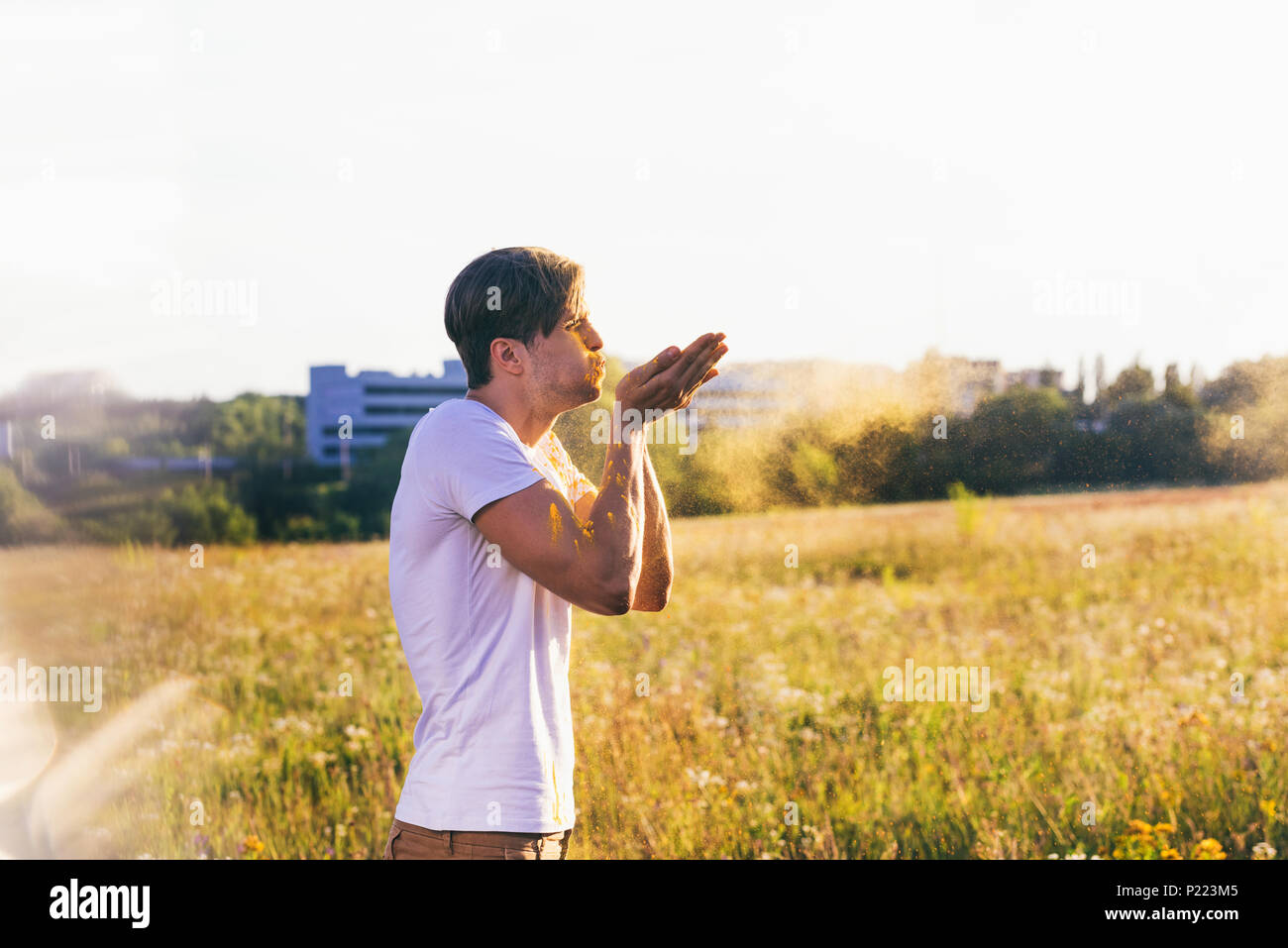 side view of man blowing colorful powder away of hands at holi festival ...