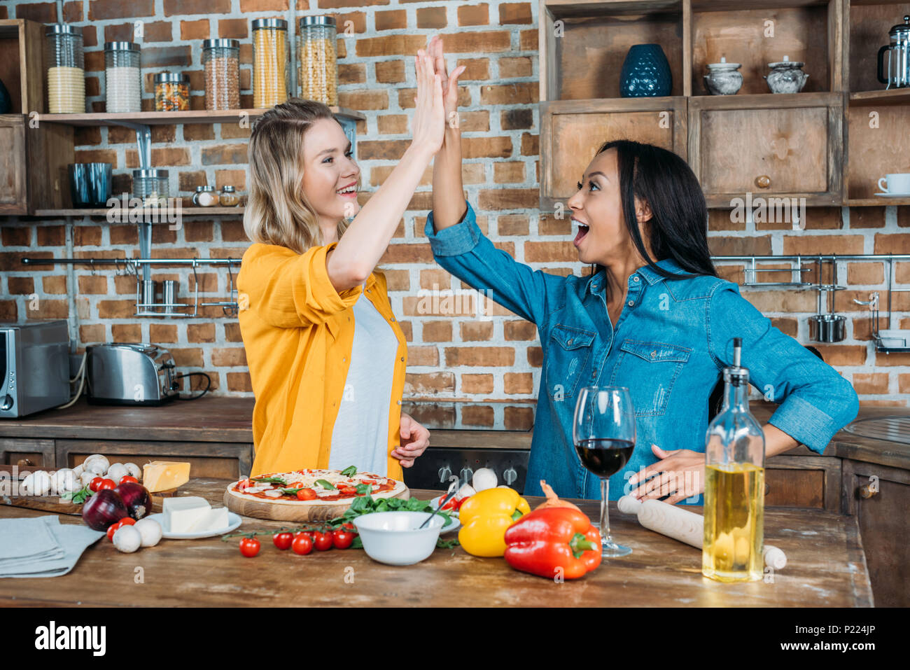 Cheerful young miltiehnic women giving high five while cooking in ...