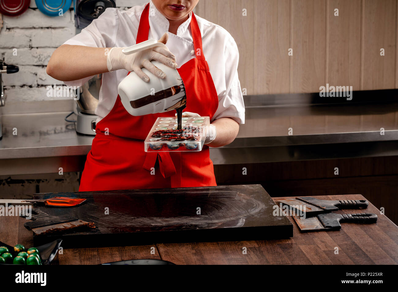 A woman confectioner with red uniform and white sterile gloves do a set ...