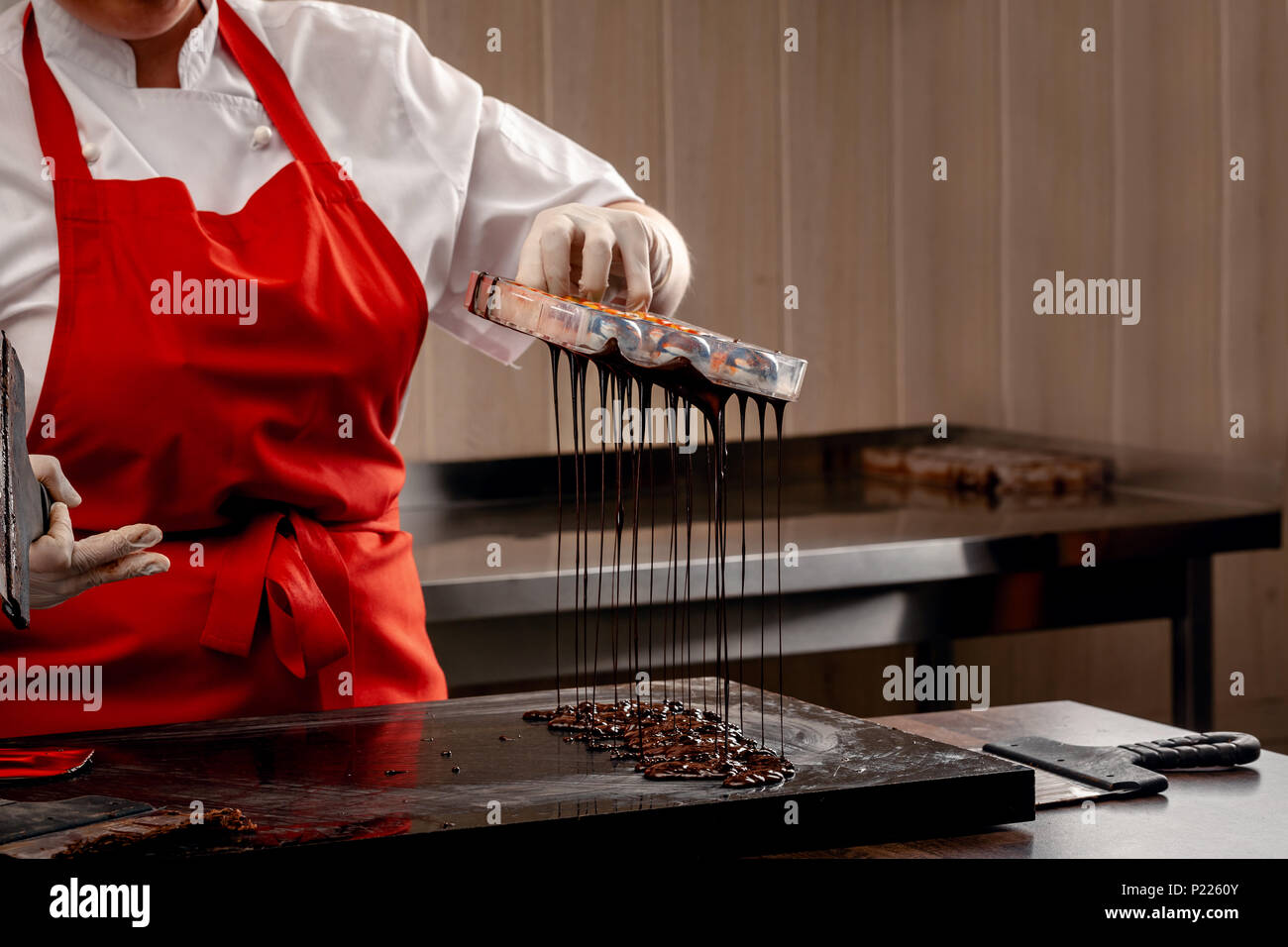 A woman confectioner with red uniform and white sterile gloves do a set ...