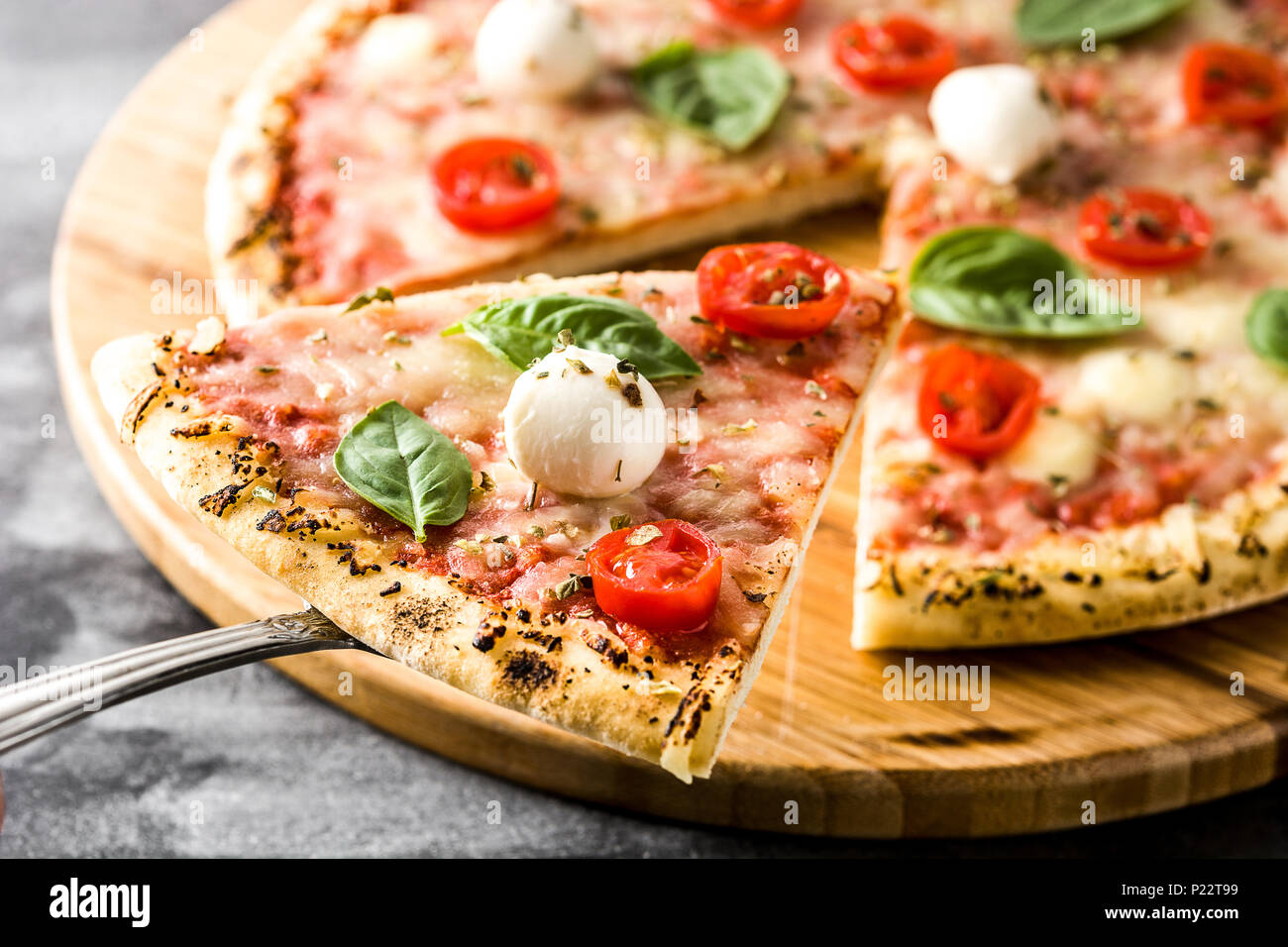 Italian pizza slice with tomatoes, cheese and basil on black stone ...