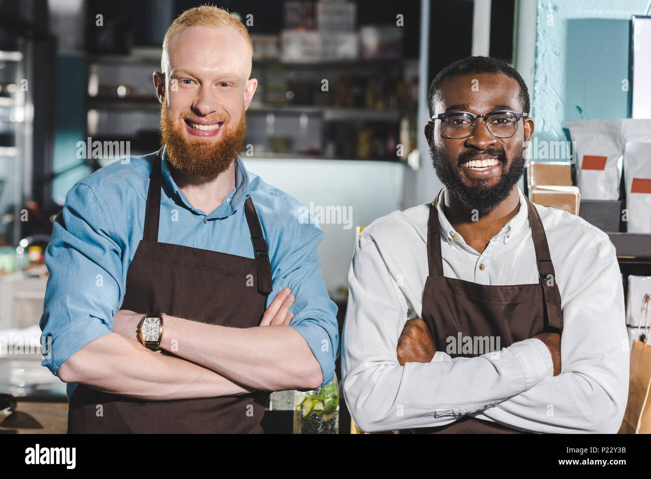 portrait of two young multiethnic owners of coffee shop in aprons ...