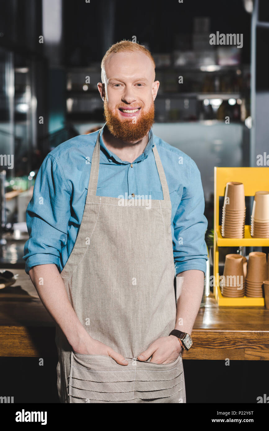 smiling young male barista in apron standing in coffee shop Stock Photo ...