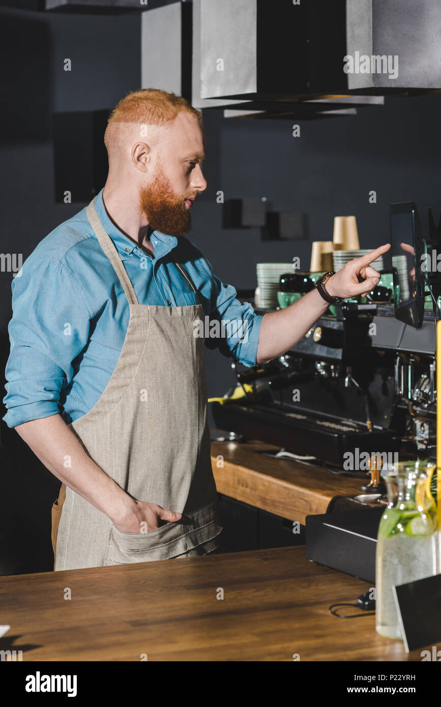 side view of handsome young barista pointing at screen while working in ...
