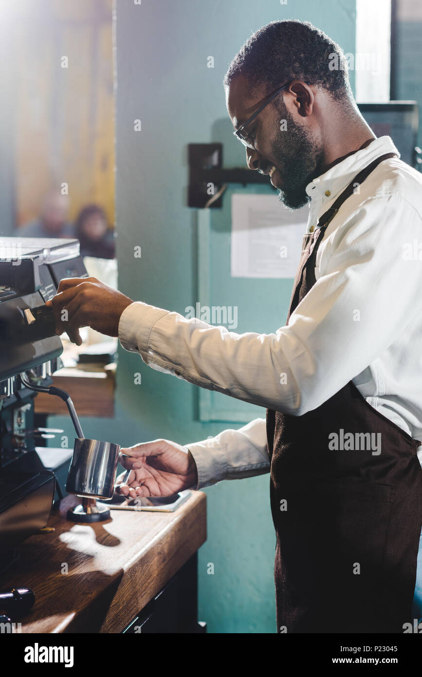 side view of happy young african american barista in eyeglasses making ...