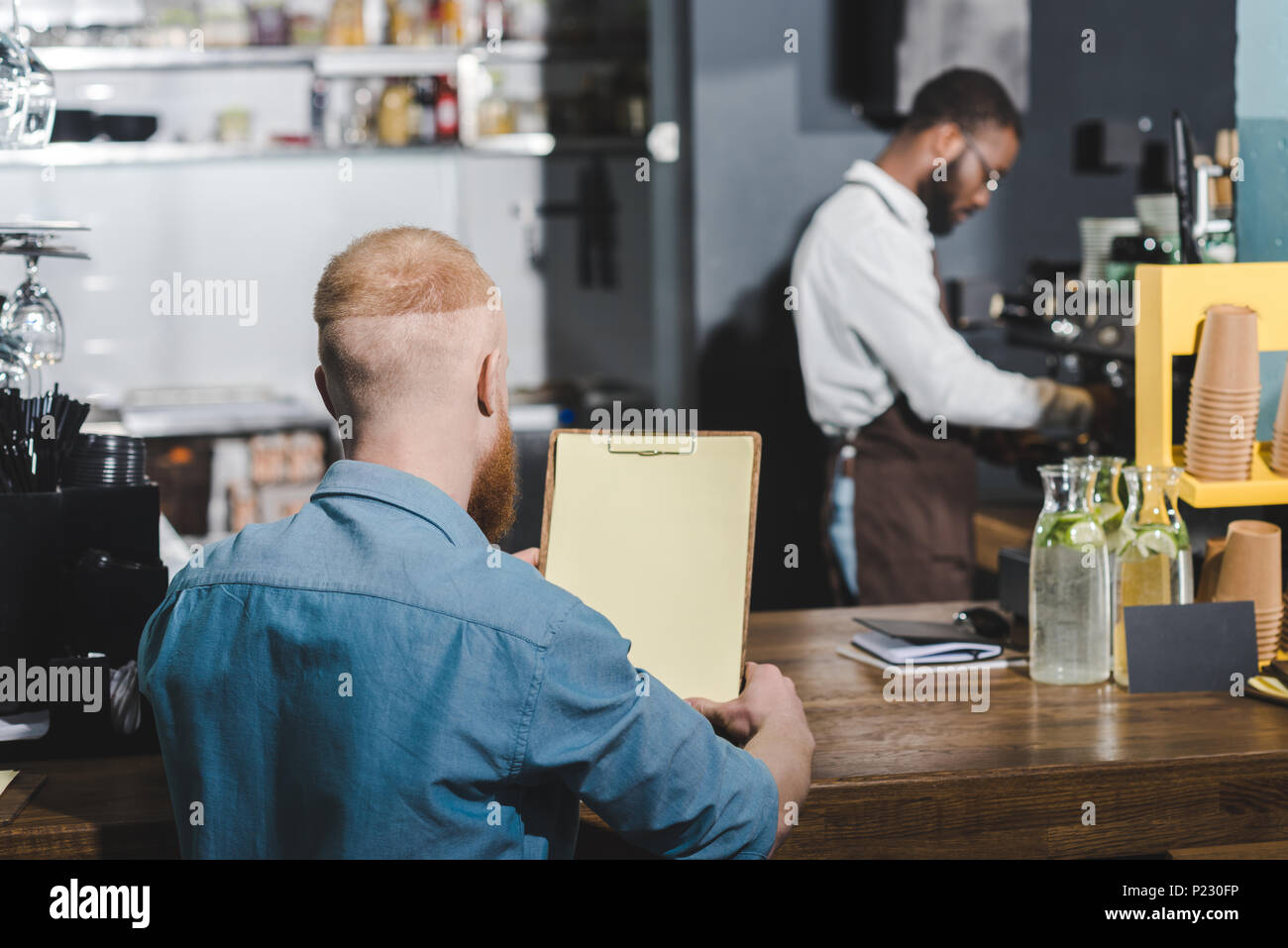 rear view of young man holding blank clipboard while barista making ...