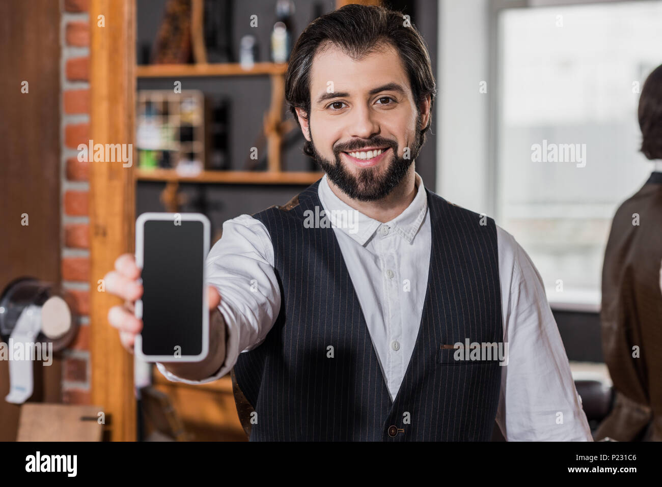 smiling young barber in vest pointing at smartphone Stock Photo - Alamy