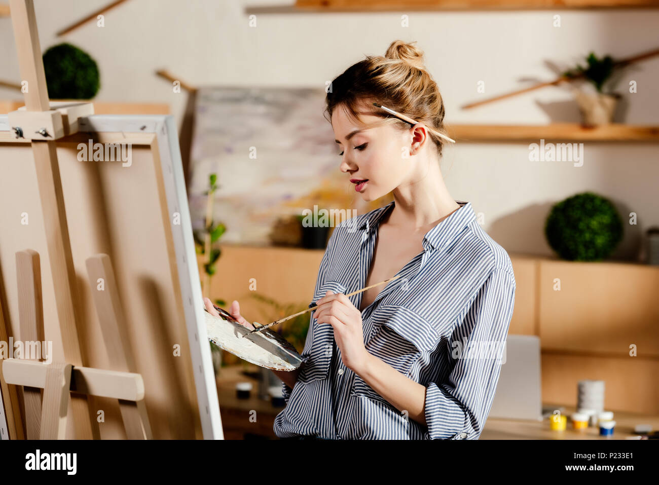 female artist with paintbrush behind ear drawing picture in studio ...