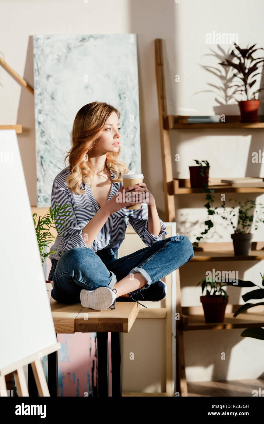 empty paper on easel and female artist sitting on table with disposable ...