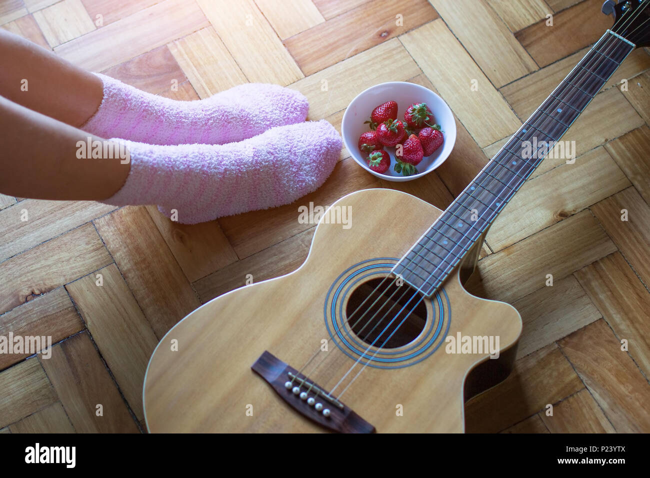 On the parquet floor - guitar, a сup of strawberries and female feet in ...