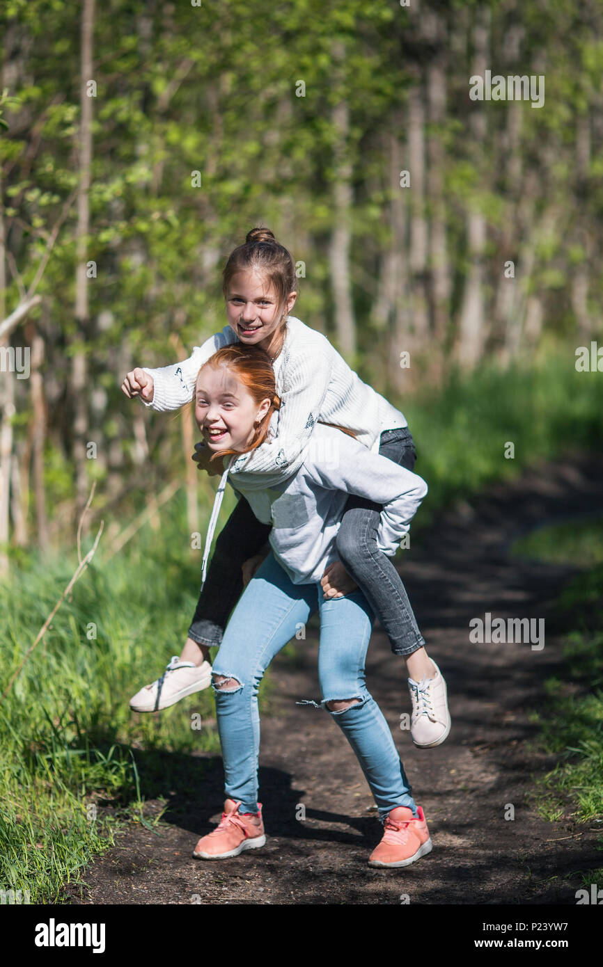 Two sisters girls friends teenagers riding each other having fun in the ...