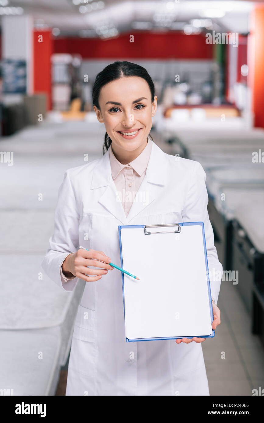 smiling shop assistant in white coat pointing at empty notepad in hand ...