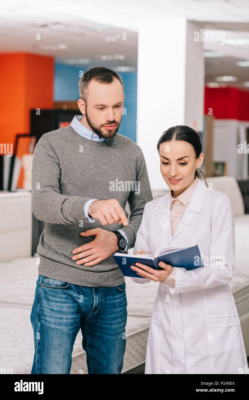 female shop assistant in white coat with notebook helping customer in ...