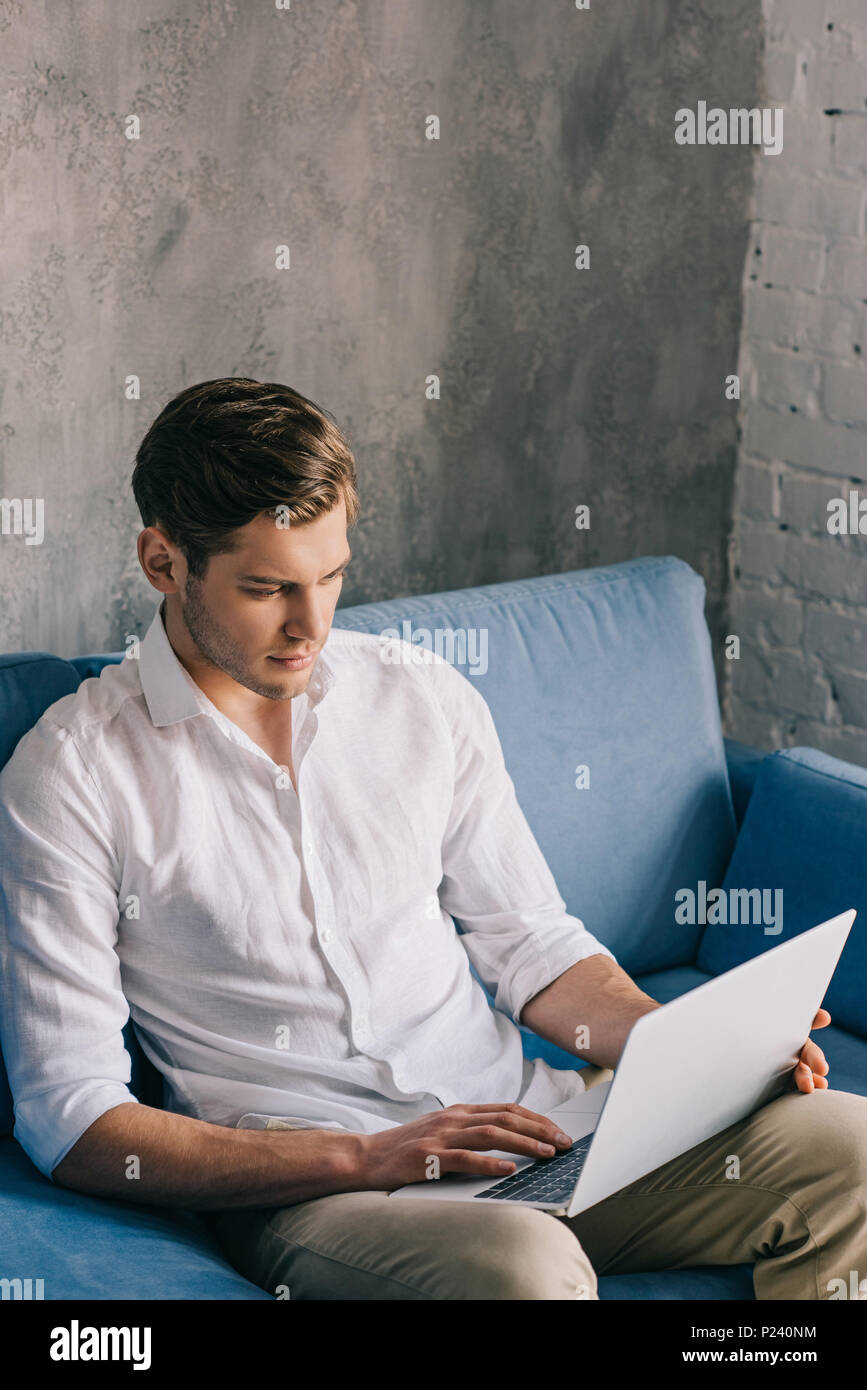 Man typing on laptop keyboard on his knees while sitting on sofa Stock ...