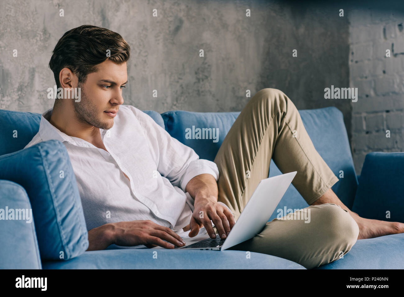 Man typing on laptop keyboard while lying on sofa Stock Photo - Alamy