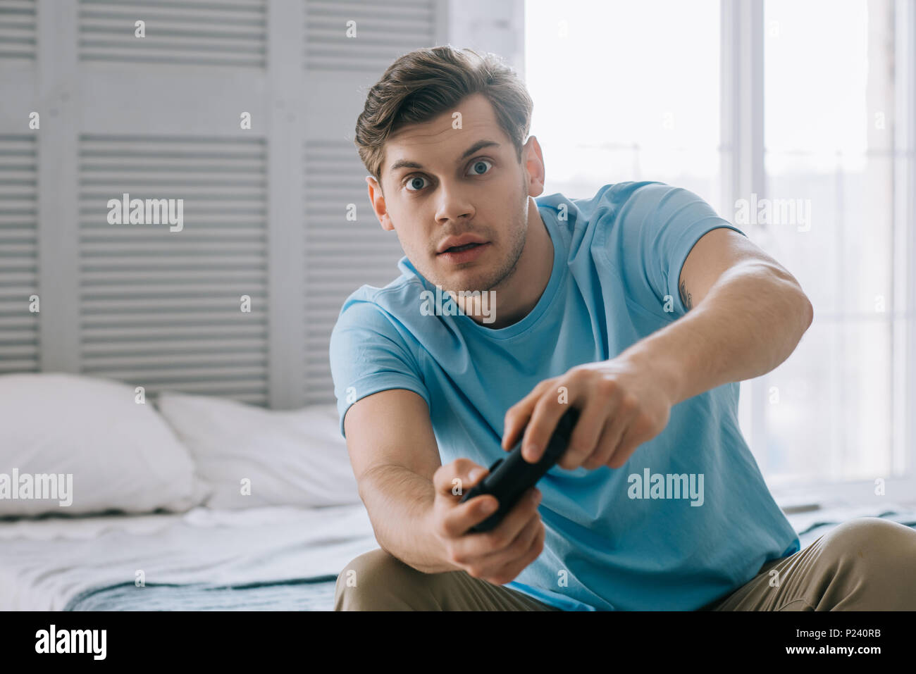 Surprised young man with joystick playing video game while sitting on ...