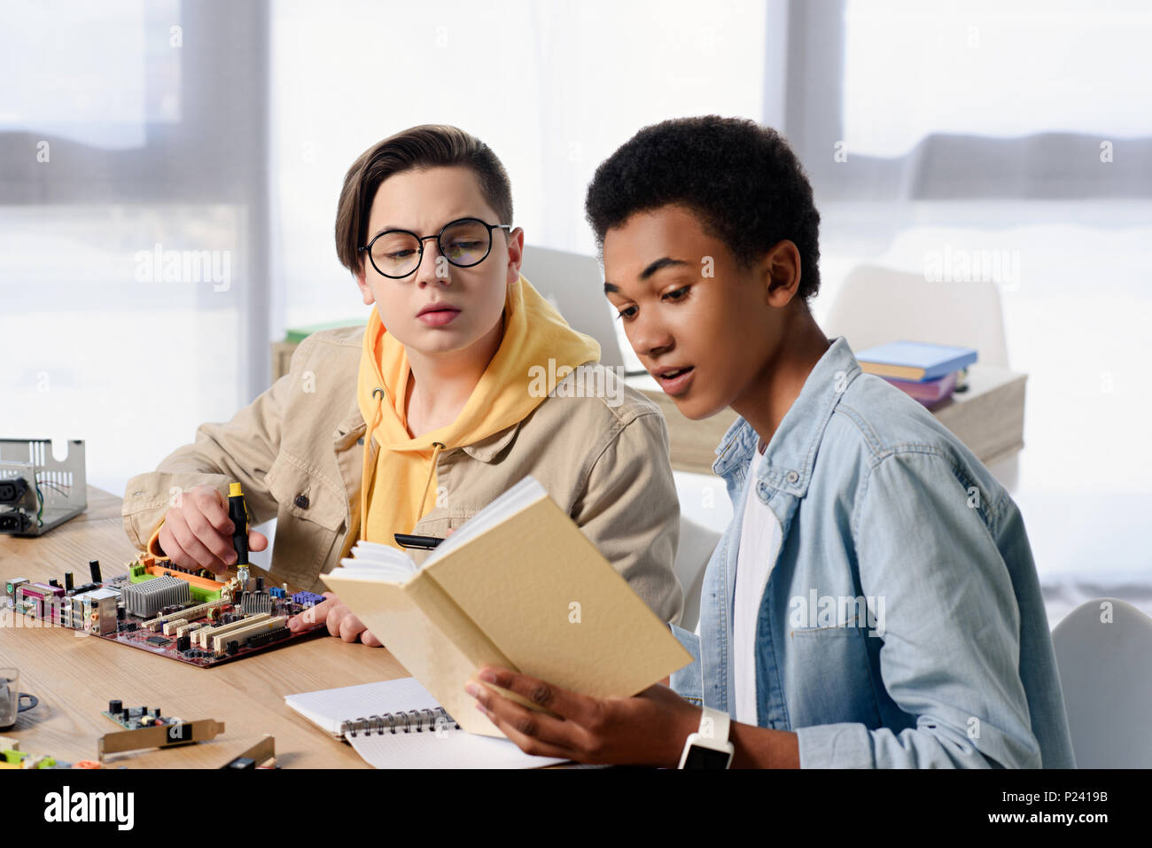 multicultural teen boys reading book about soldering motherboard at ...