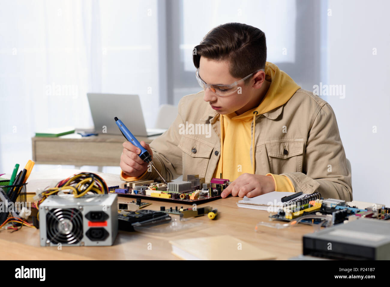 teen boy soldering computer motherboard with soldering iron at home ...