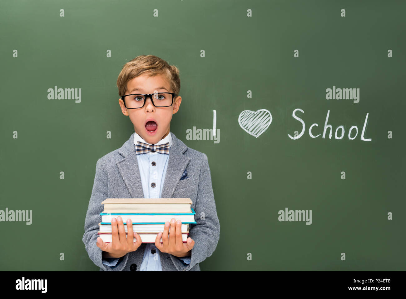 shocked schoolboy with stack of books next to chalkboard with i love ...