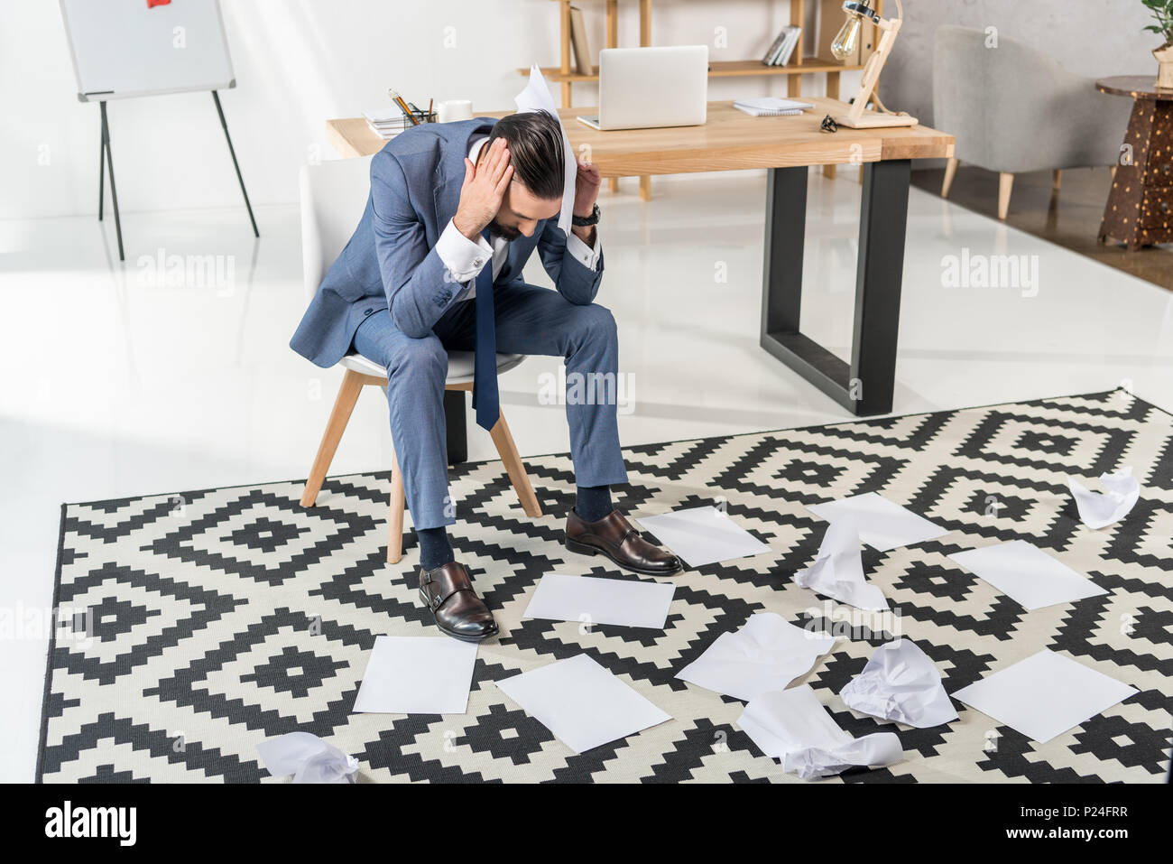 stressed businessman sitting on chair and looking at papers on floor in ...