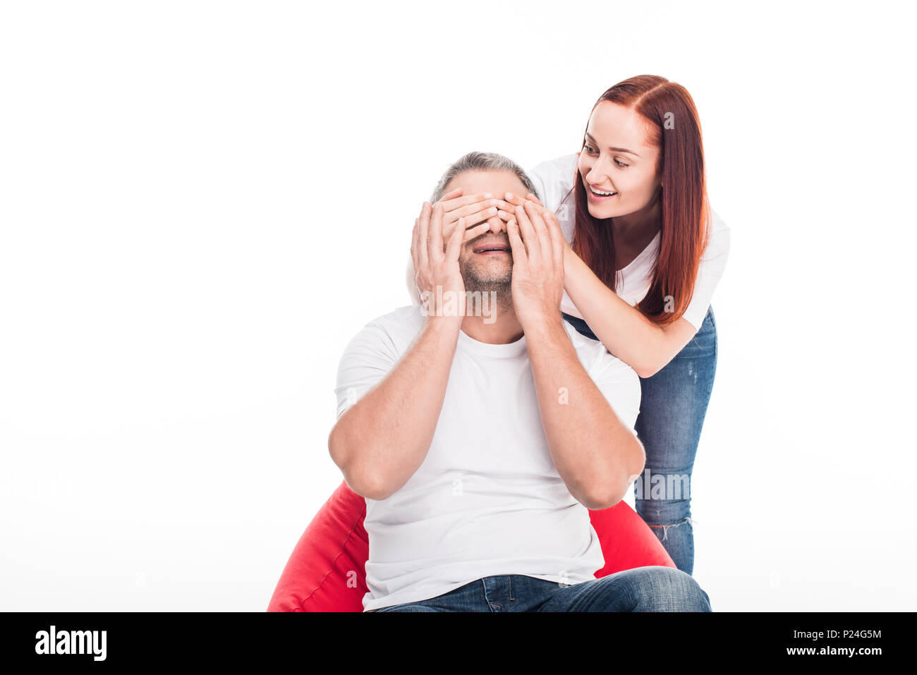 smiling woman closing eyes of her surprised husband, isolated on white ...