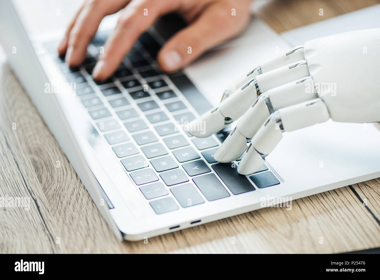 close-up view of human and robot hands typing on laptop at workplace ...