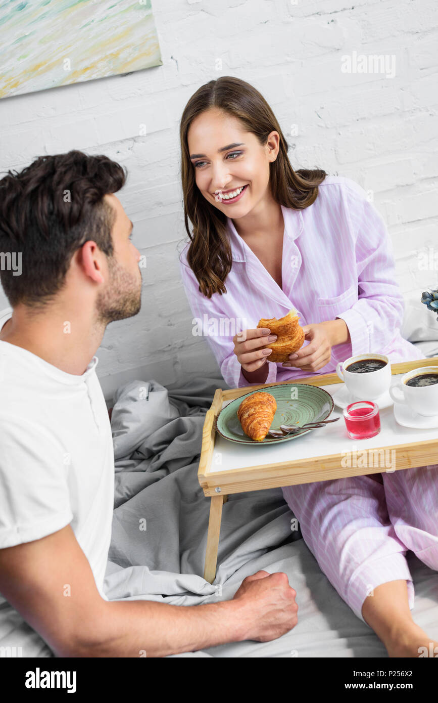 young laughing couple in pajamas having breakfast with coffee and ...