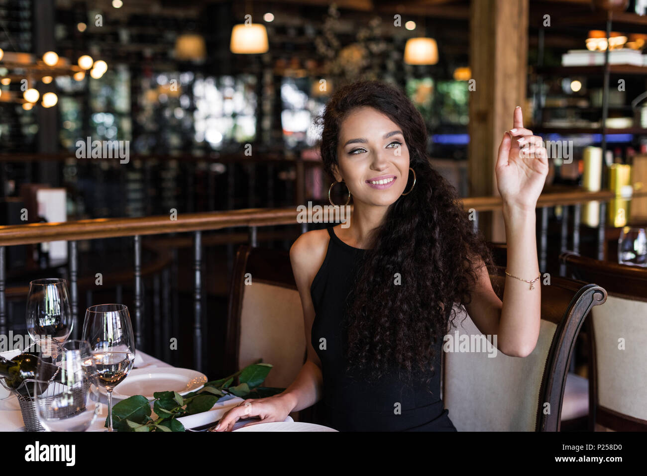 Portrait of young beautiful woman with raised hand calling waiter in ...