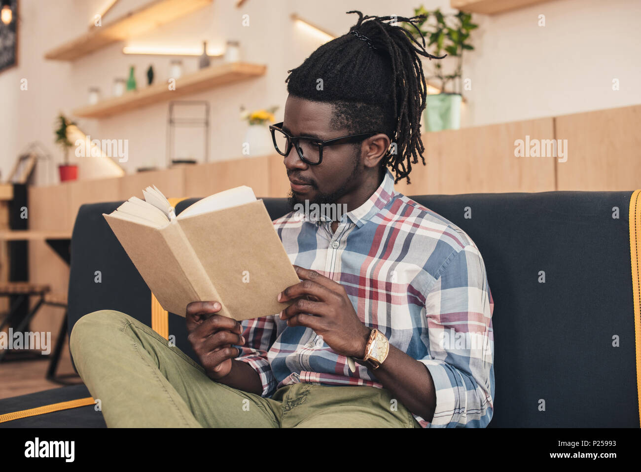african american man reading book while sitting on sofa in cafe Stock ...