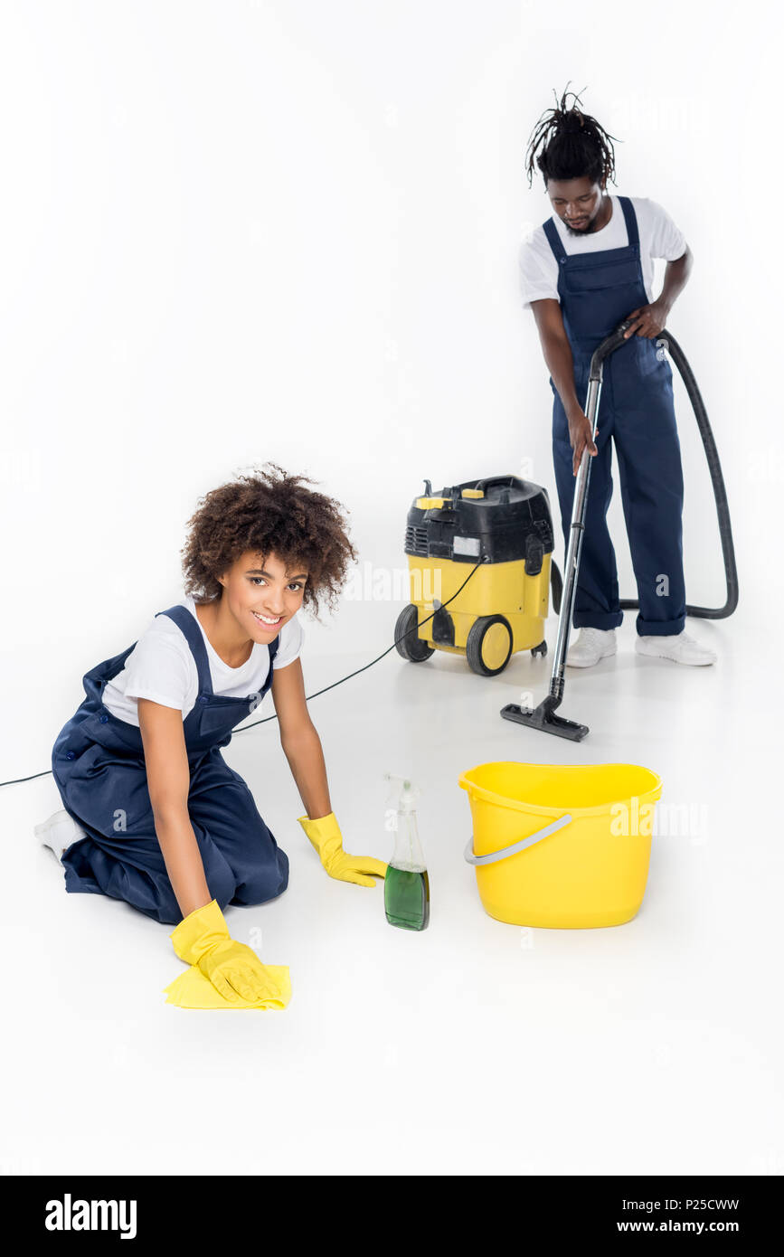 african american cleaners in uniform with cleaning supplies looking at ...