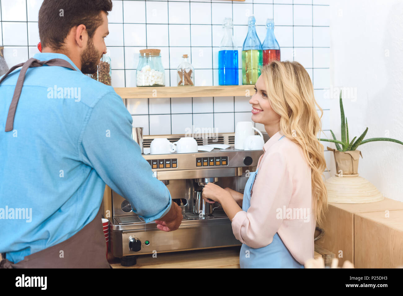 smiling young couple of cafe workers making coffee together and using ...
