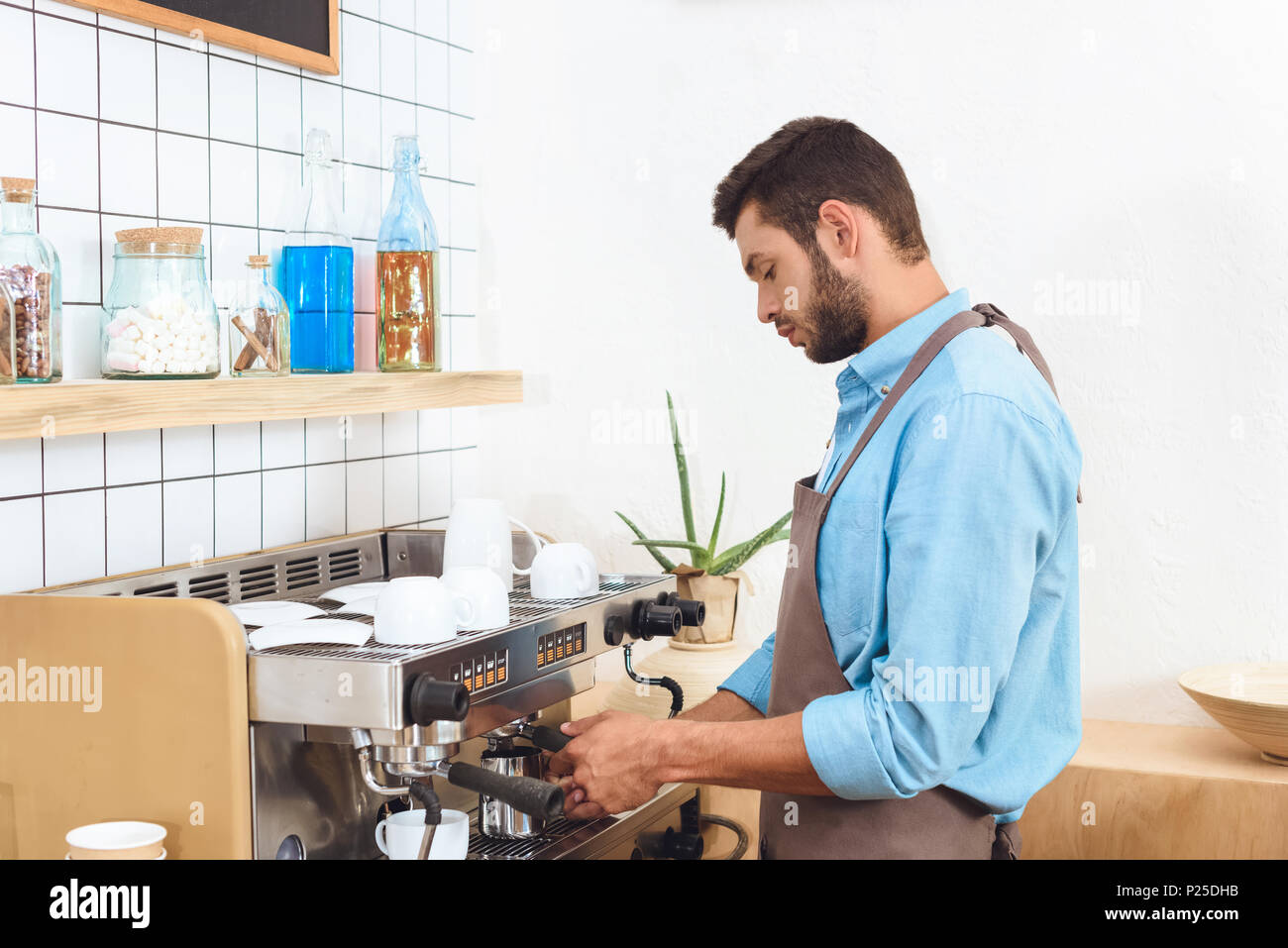 side view of young barista in apron making coffee with coffee machine ...