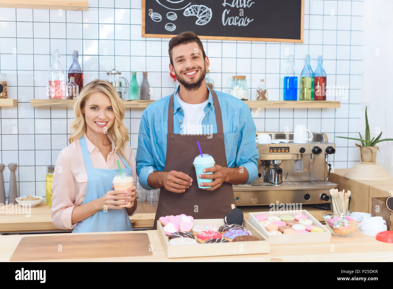 cheerful young barista and waitress holding milkshakes and smiling at ...