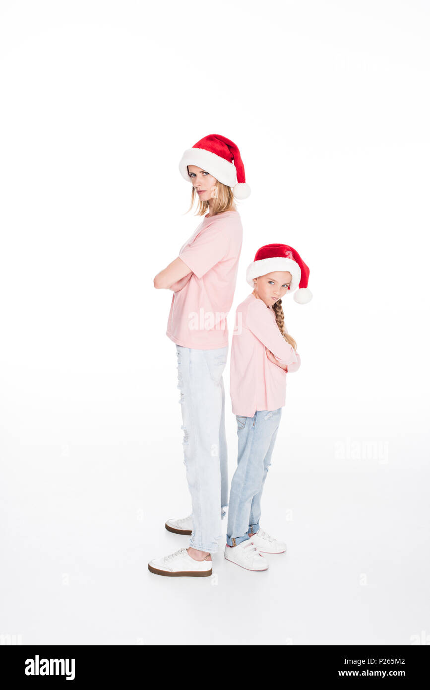 Grumpy mother and little daughter in santa hats posing with arms ...