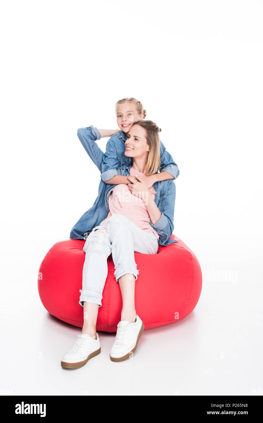 Woman sitting on a red bean bag while her daughter is hugging her ...