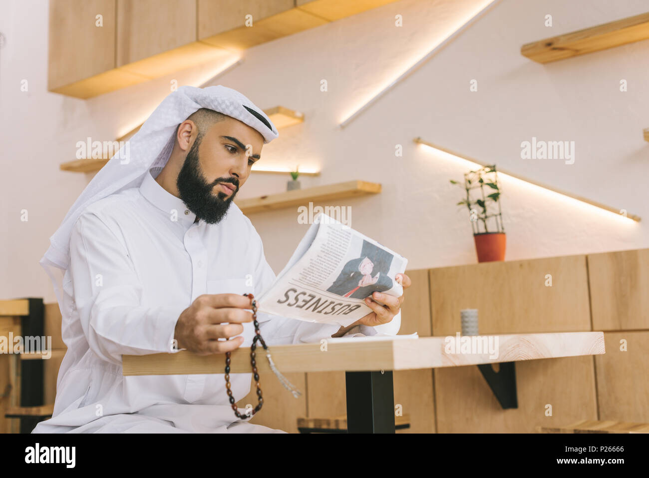 serious muslim man reading newspaper in cafe and holding prayer beads ...