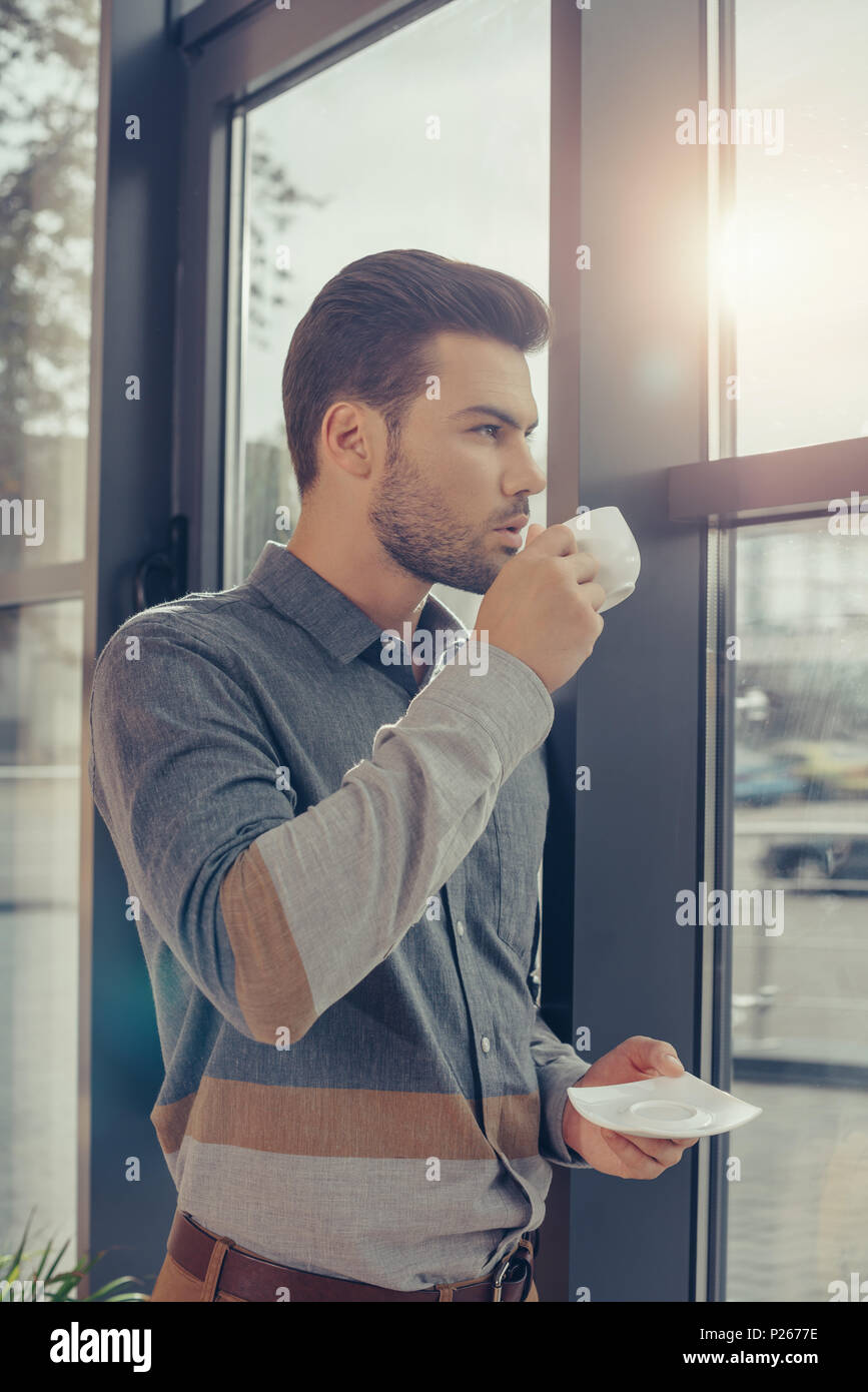 side view of thoughtful man drinking coffee and looking out window in ...