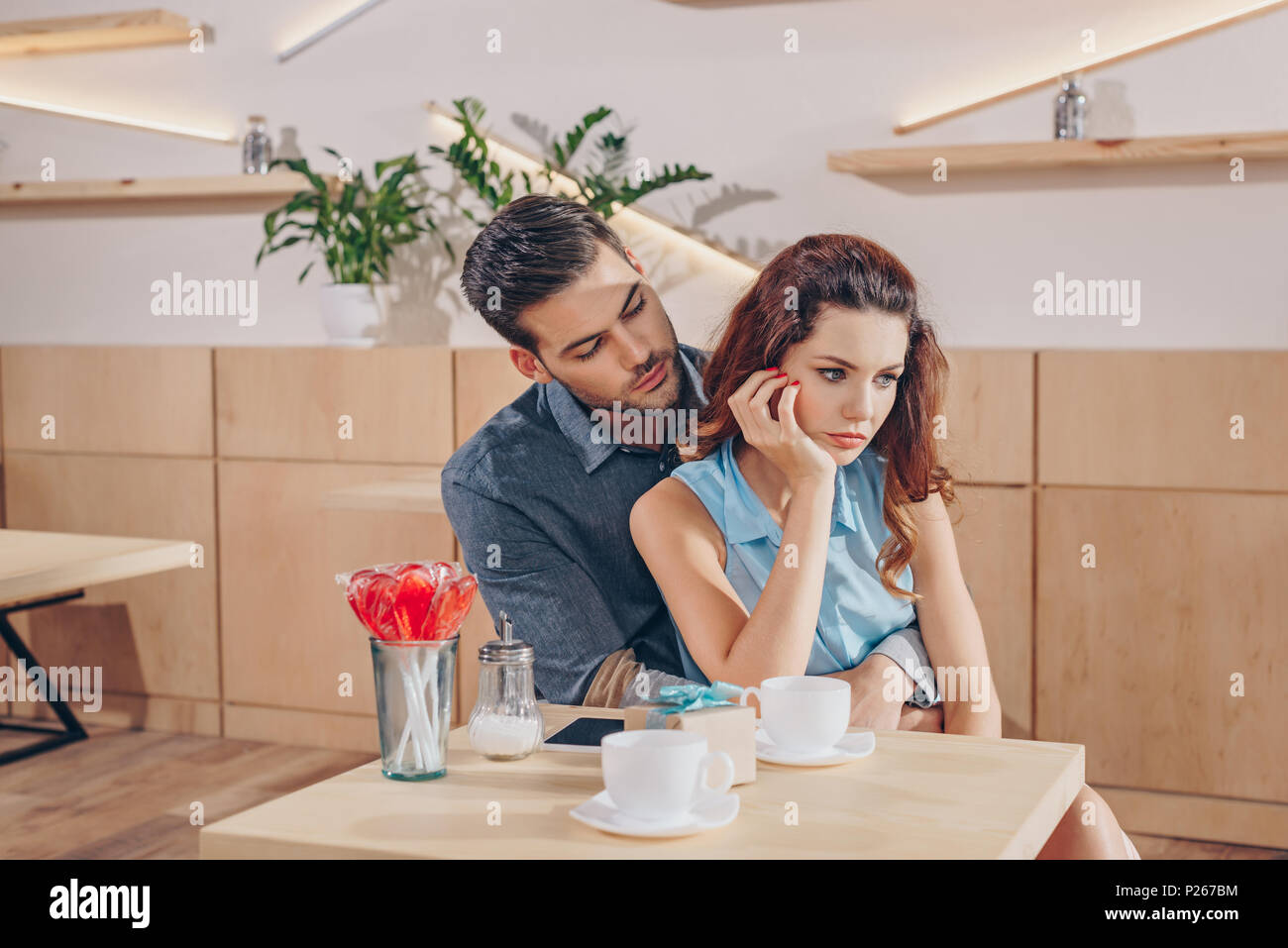 man hugging upset girlfriend while having romantic date in coffee shop ...