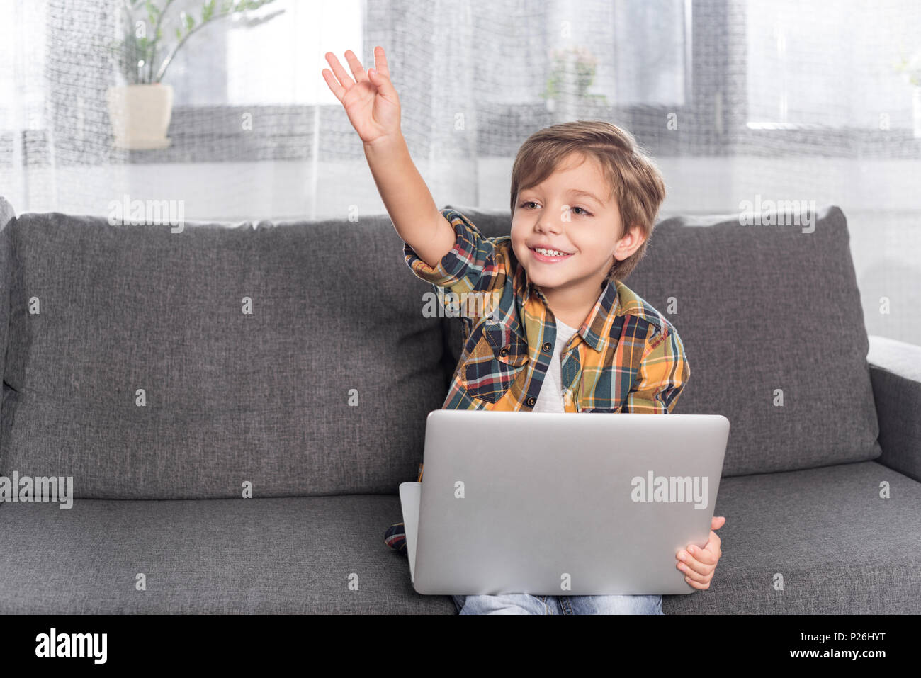 boy with laptop sitting on couch and raising hand Stock Photo - Alamy