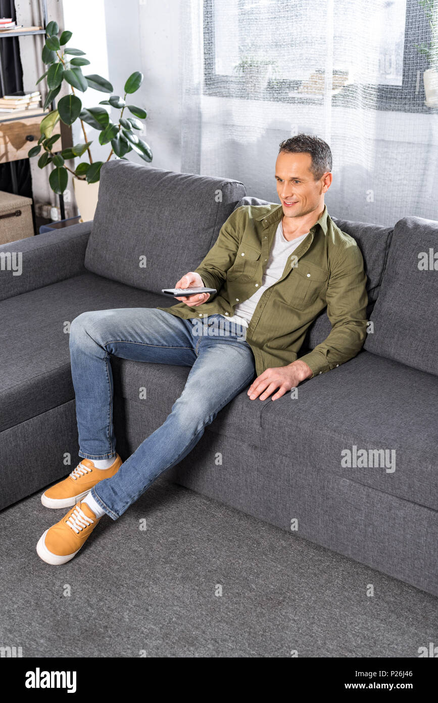 handsome adult man with tv remote sitting on couch Stock Photo - Alamy