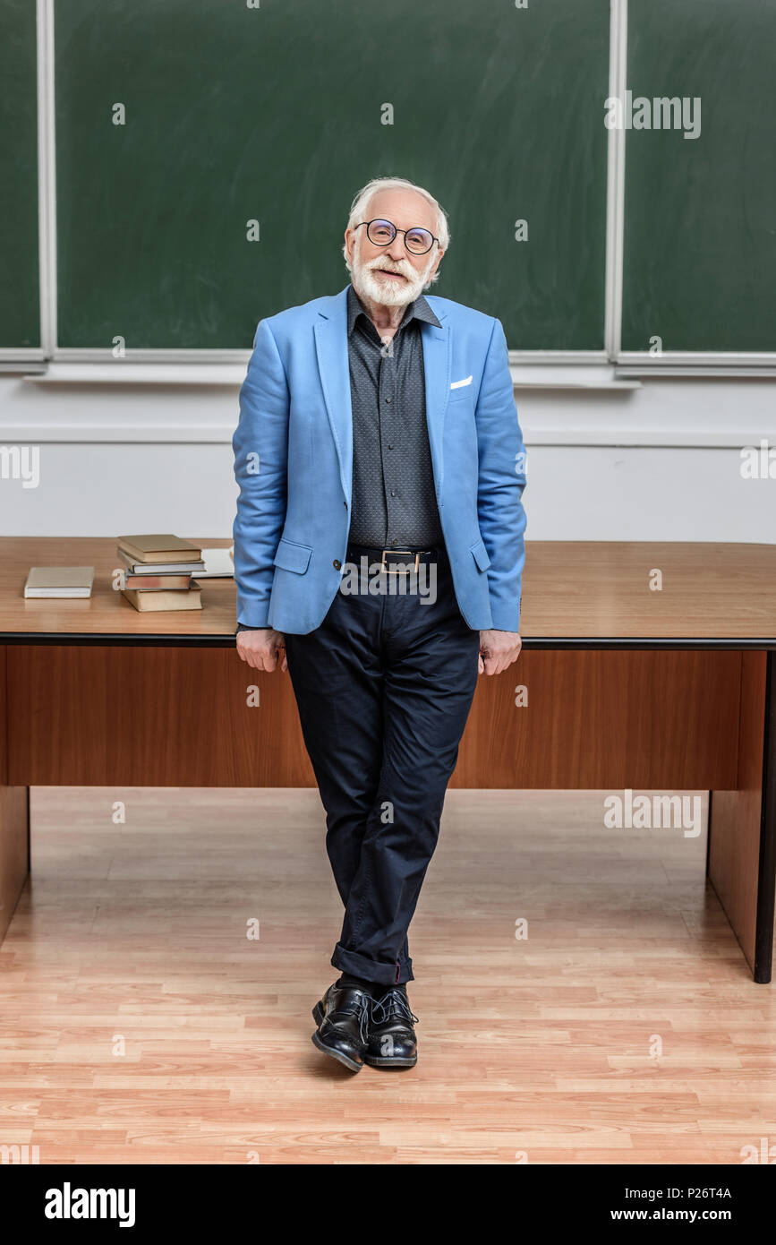 grey hair professor standing in lecture room and looking at camera ...