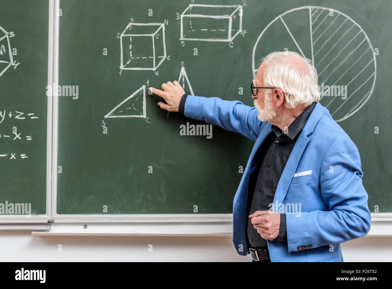 grey hair professor pointing on something with finger at blackboard ...