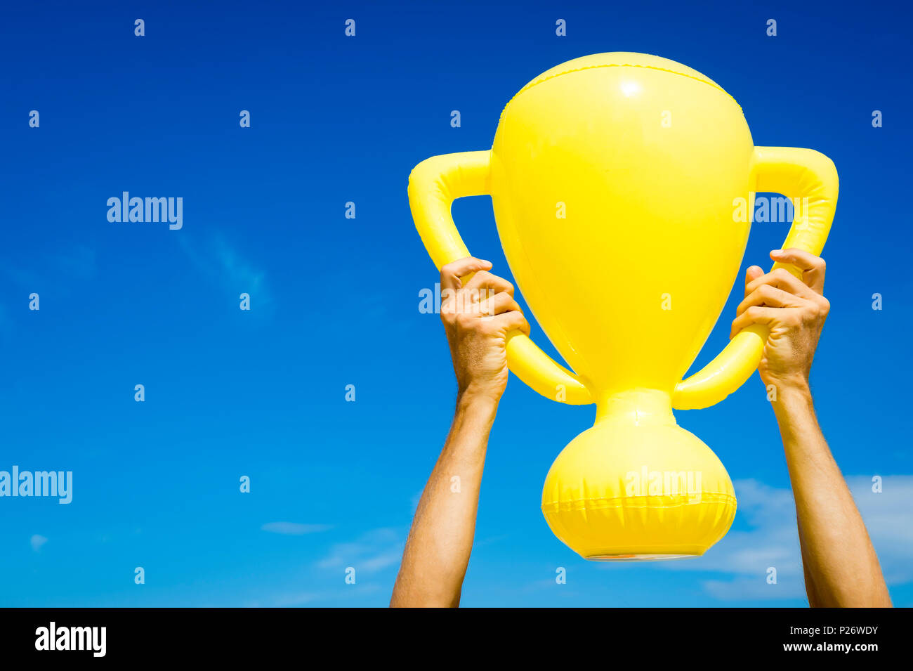 Hands holding aloft an inflatable yellow trophy in bright blue sky ...