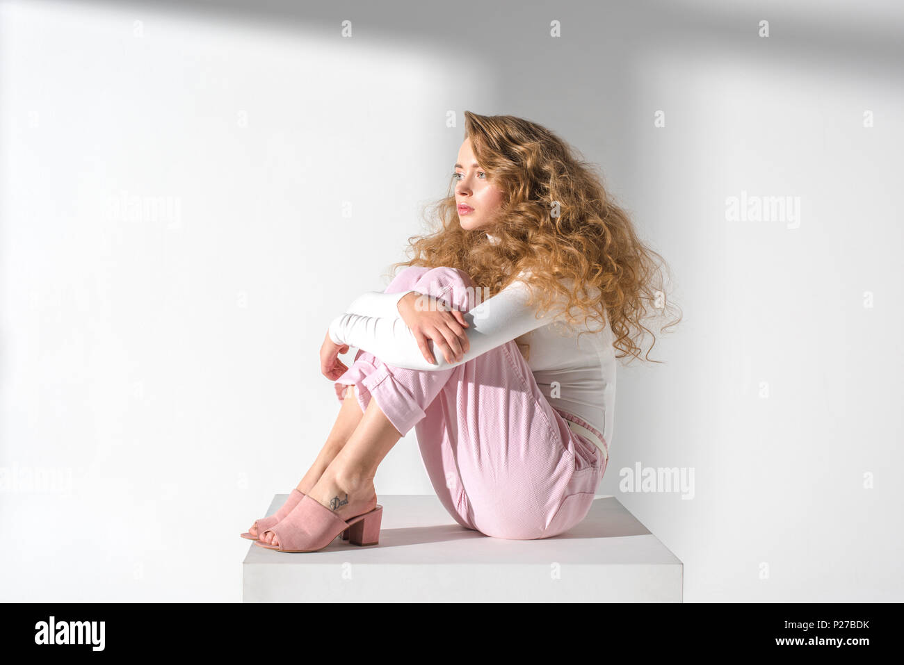 Upset girl sitting on white cube and hugging her legs Stock Photo - Alamy