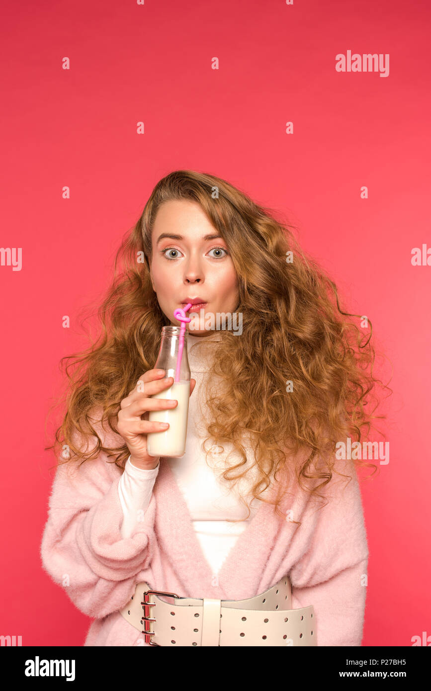 surprised girl drinking milkshake with plastic straw isolated on red ...