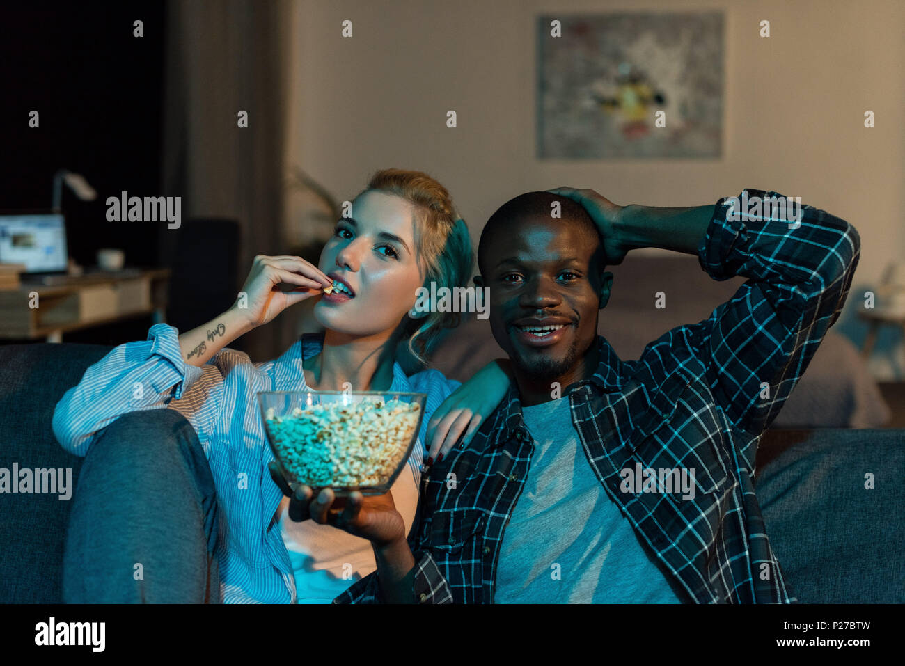 portrait of multiethnic couple eating popcorn and watching film ...