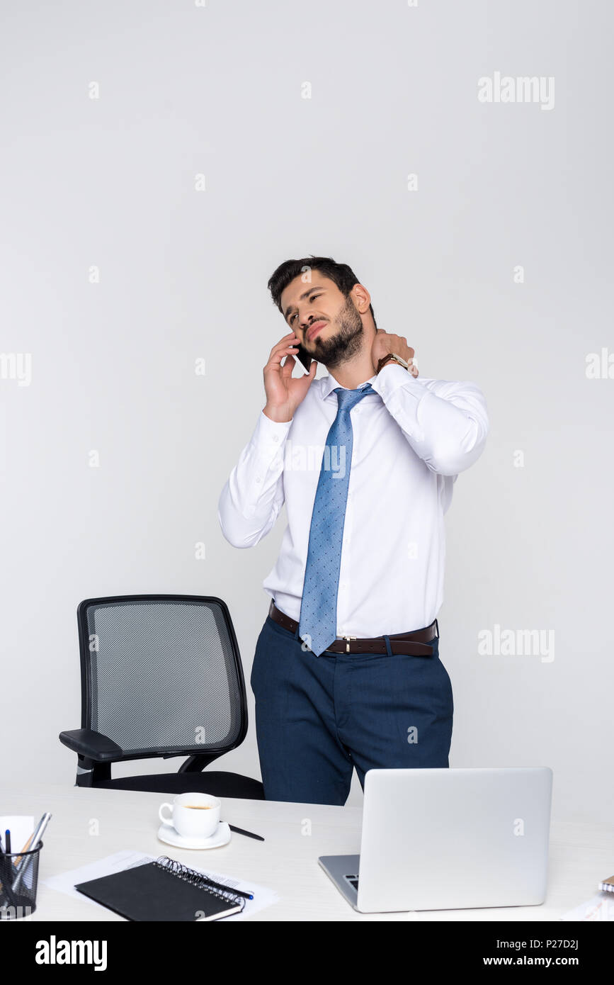young overworked businessman suffering from pain on neck while talking ...