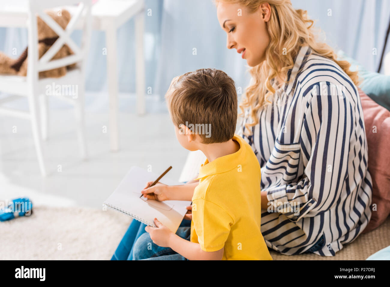 side view of young mother and son drawing picture together while ...